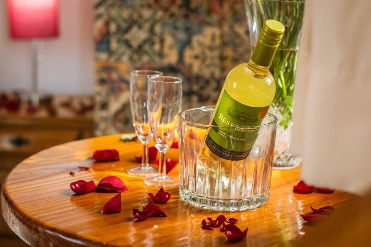 Uma garrafa de vinho Conchator sobre uma mesa de madeira, com copos e pétalas de rosa.