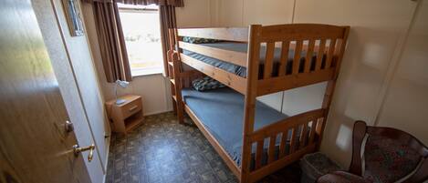 Quarto com beliche, janela, cadeira e pequena mesa.