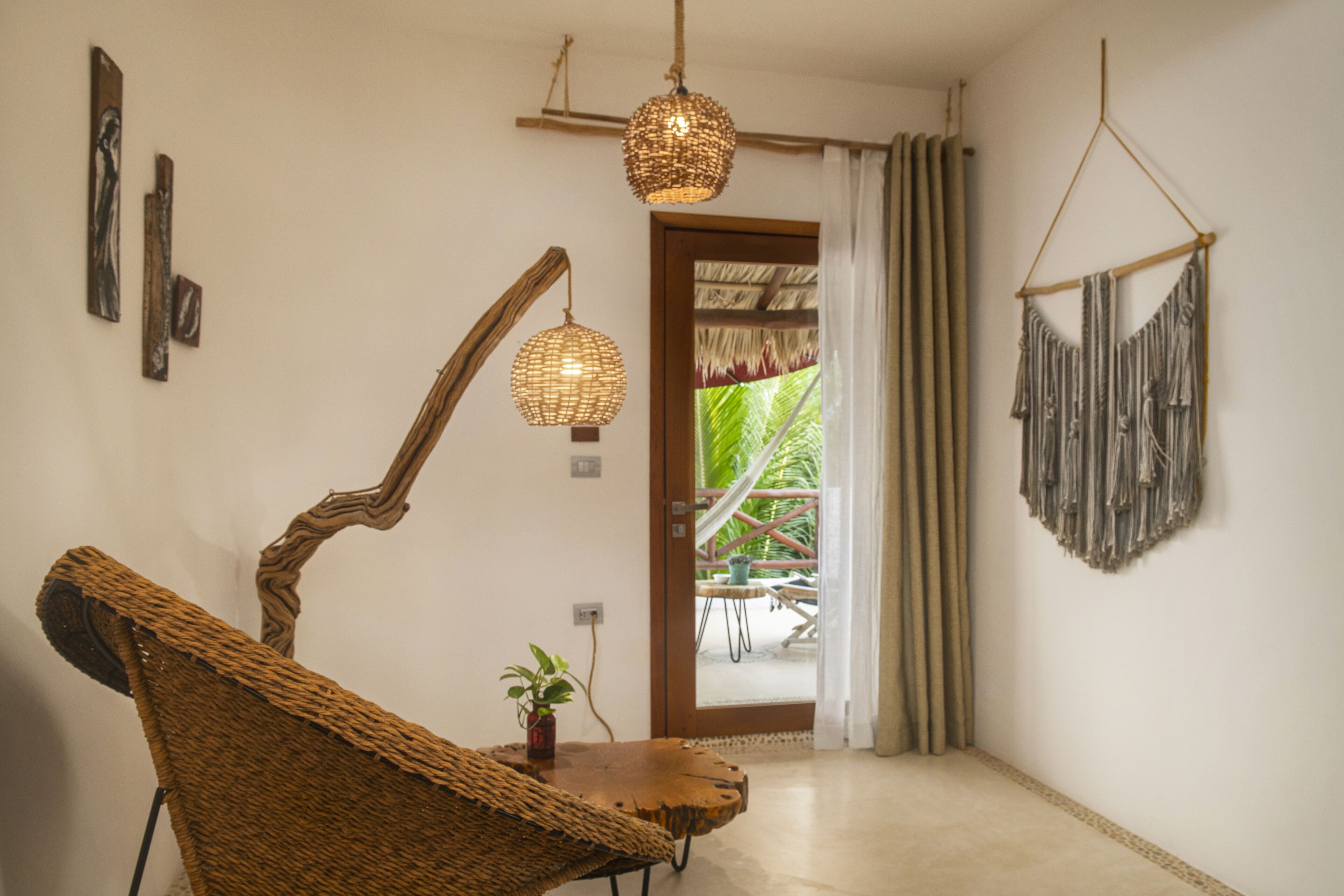 Um quarto com uma cadeira de fibra natural, uma luminária pendente e um painel têxtil na parede.