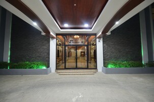 Entrada de um edifício moderno com porta de vidro, teto de madeira e escada para o interior.