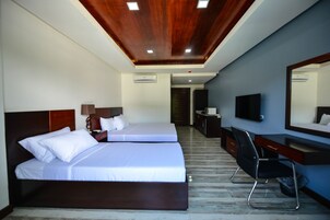 Quarto de hotel com duas camas, uma escrivaninha, uma cadeira, televisão e espelho.
