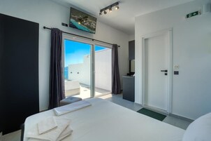 Quarto de hotel com uma cama, escrivaninha, cadeira, janela grande e porta.