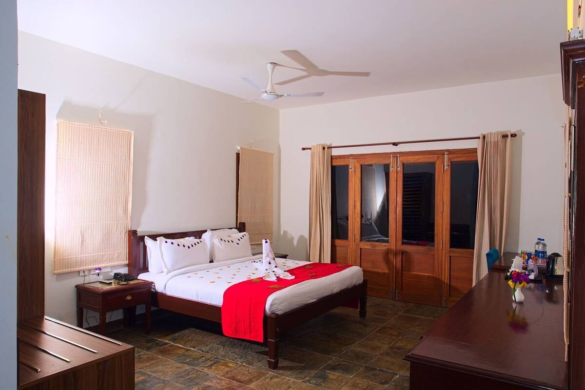 Quarto com cama, guarda-roupa de madeira, escrivaninha e ventoinha no teto.