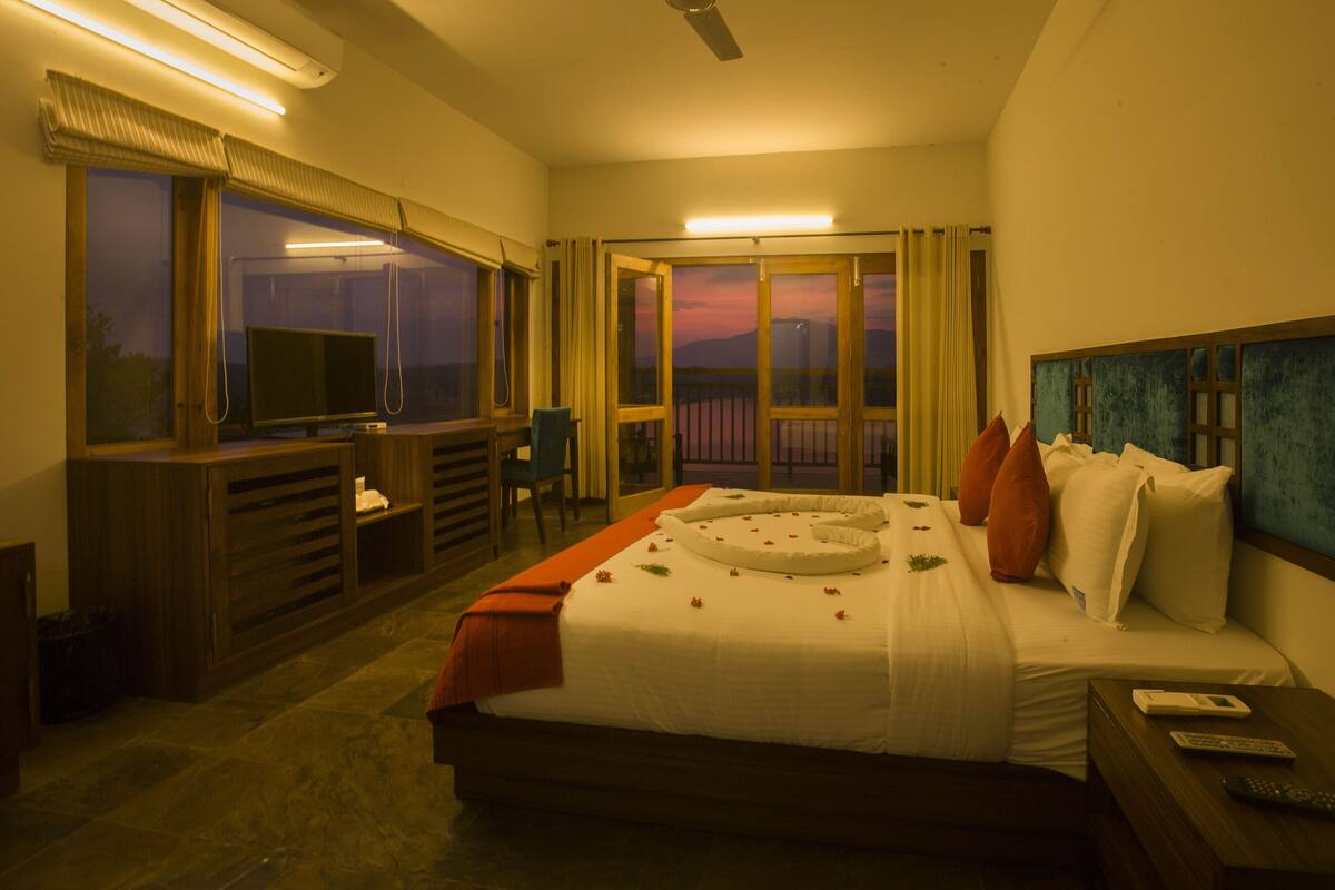 Quarto de hotel com cama, televisão, escrivaninha e varanda com vista.