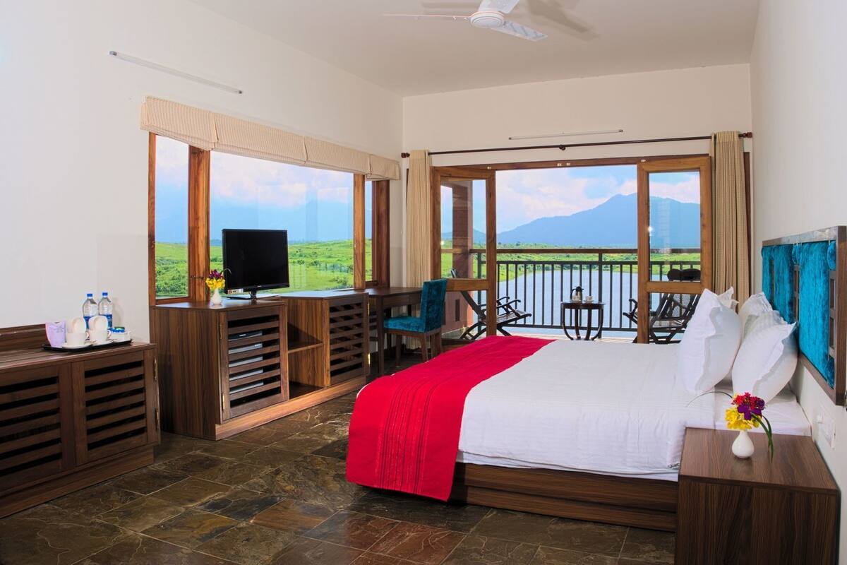 Quarto com cama, TV, escrivaninha e varanda com vista.