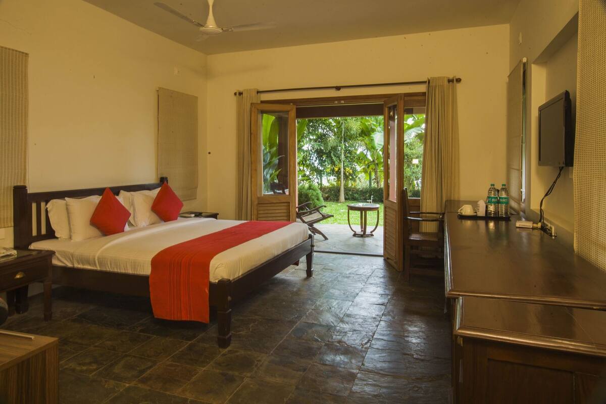 Quarto de hotel com cama, escrivaninha, cadeira, televisão e vista para o exterior.