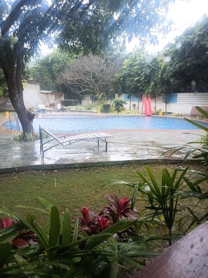 Piscina com escorrega, cercada por vegetação exuberante e um deck revestido com azulejos.