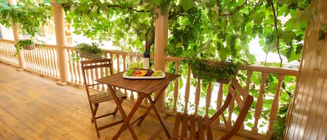 Um deck de madeira com mesa e cadeiras, cercado por vegetação exuberante e um corrimão de madeira.