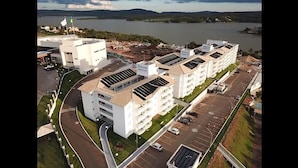 Vista aérea de um complexo moderno de edifícios, com vários edifícios brancos, painéis solares nos telhados e um estacionamento.