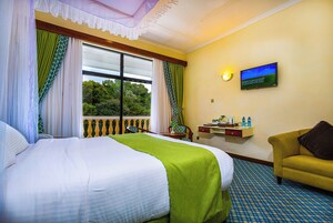 Quarto de hotel com cama, televisão, sofá e varanda com cortinas.