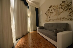 Uma sala de estar com um sofá cinzento, um mural na parede e uma janela com cortinas.