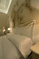 Quarto de hotel com uma cama, mesa de cabeceira com abajur, espelho e um mural decorativo na parede.
