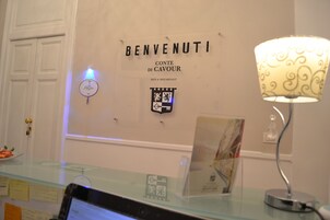 Uma área de recepção com uma placa 'BENVENUTI', um brasão e um abajur.
