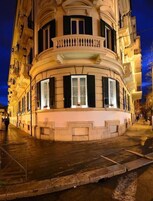 Um edifício histórico com fachada curva, janelas grandes com persianas e uma varanda com grades.