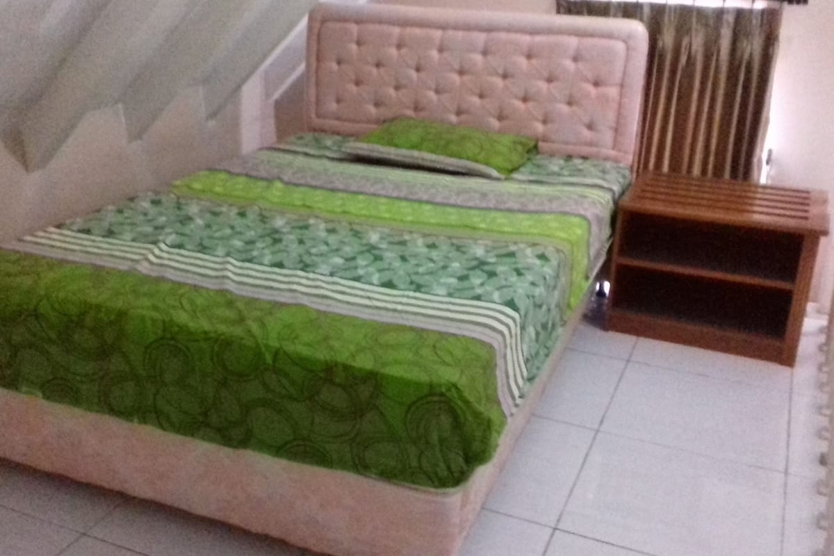 Quarto com cama, mesa de cabeceira e janela com cortinas.