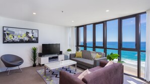 Sala de estar moderna com uma televisão grande, assentos confortáveis, uma mesa de centro e vista para o oceano.