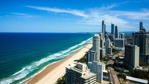 Paisagem costeira urbana com edifícios altos, uma praia e um céu azul límpido.