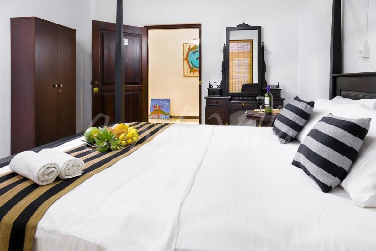 Quarto de hotel com cama, armário, escrivaninha com espelho e um quadro na parede.