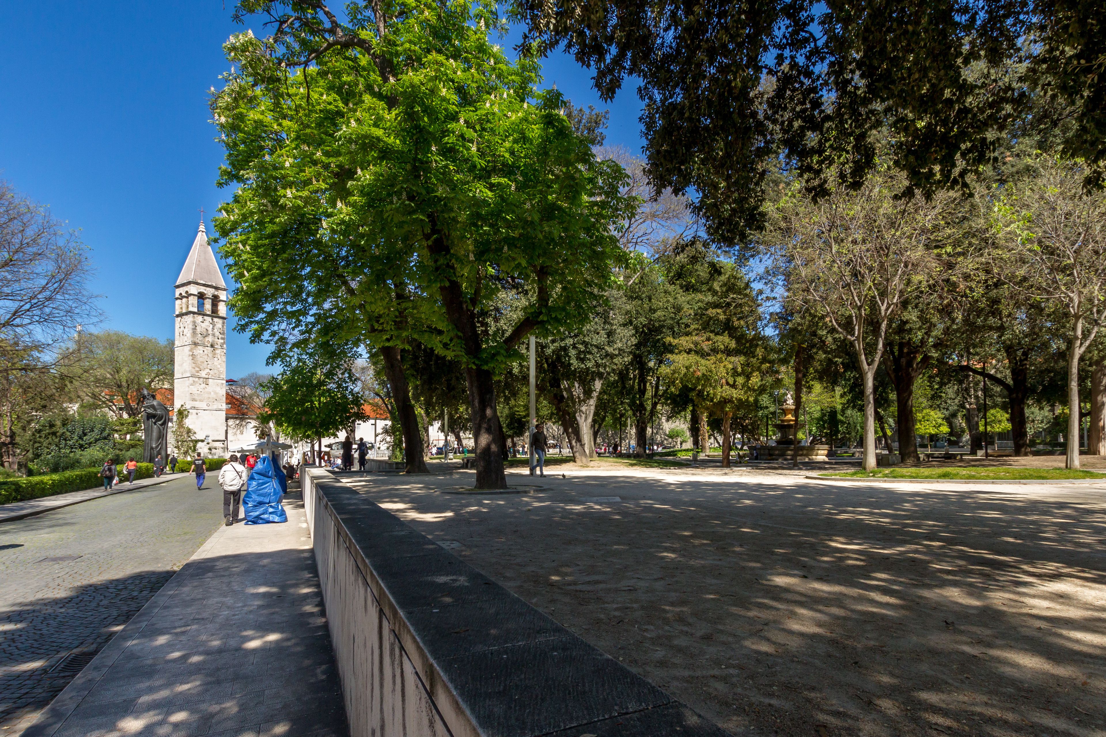 Um parque com uma torre alta, árvores e um caminho pavimentado.