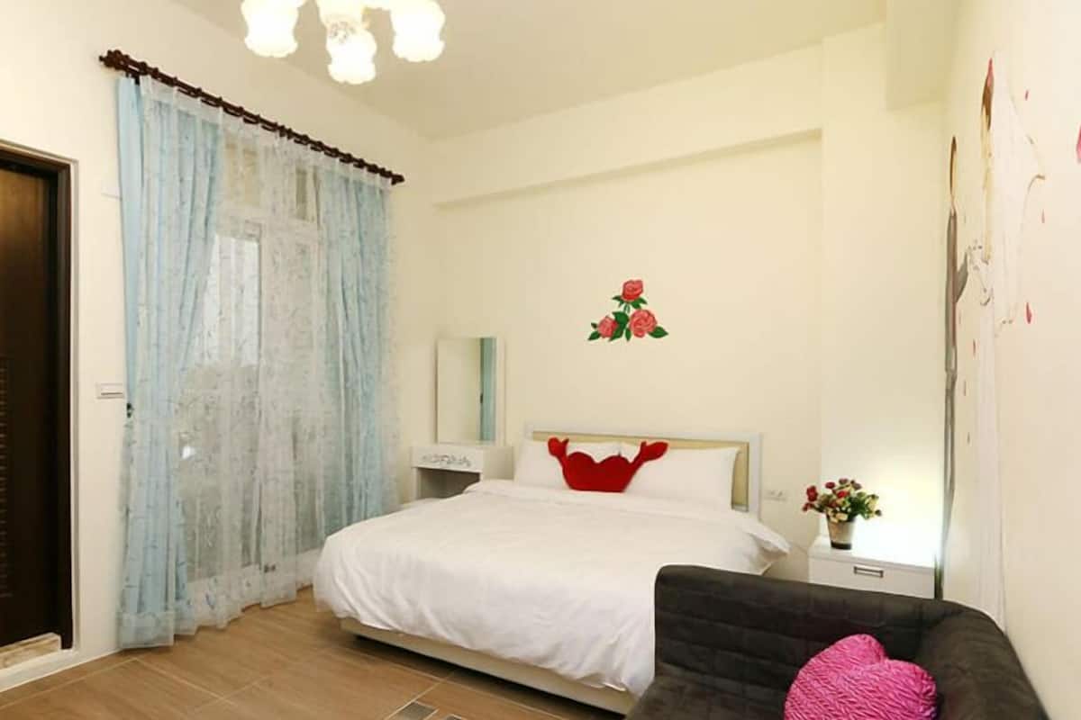 Um quarto com cama, mesa de cabeceira, penteadeira, porta e janela com cortinas.