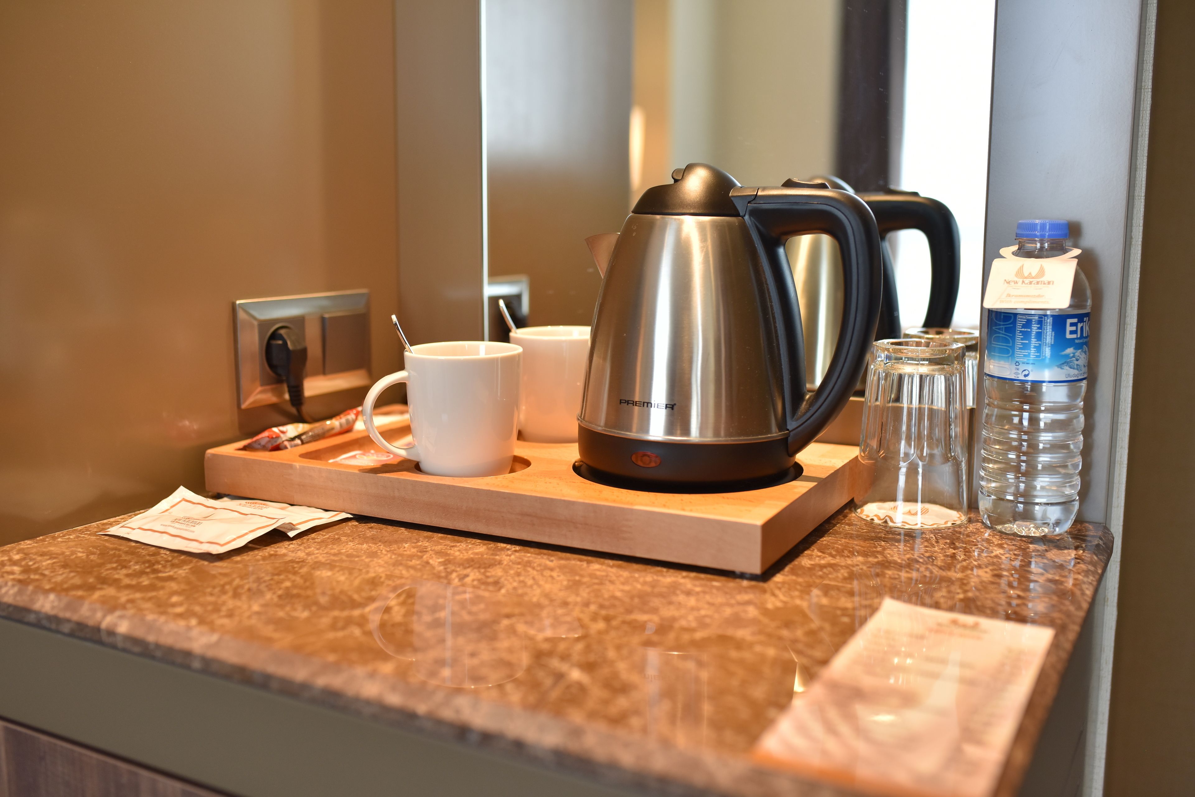Uma cozinha de hotel compacta com cafeteira, xícaras e garrafas de água em bancada de granito.
