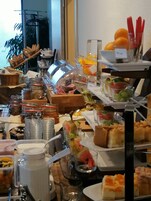 Buffet com diversos alimentos e bebidas, incluindo frutas, doces e uma estação de café.
