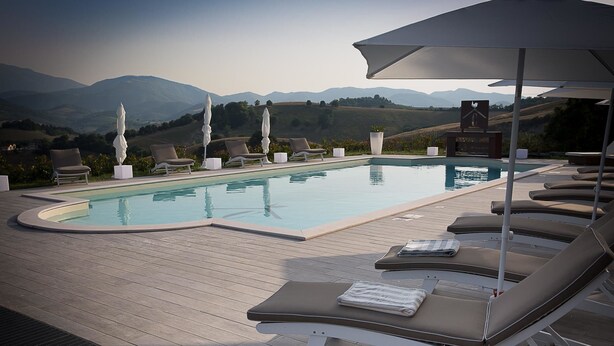 Área à beira da piscina com espreguiçadeiras, guarda-sóis e vista para montanhas.