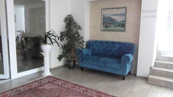 Uma sala de estar com um sofá azul, uma grande planta em vaso, um tapete estampado e um quadro na parede.