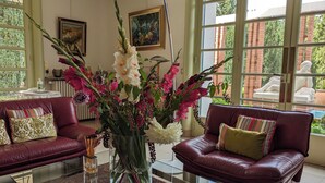 Uma sala de estar com uma mesa de centro de vidro, dois sofás de couro, um vaso com flores e um quadro na parede.