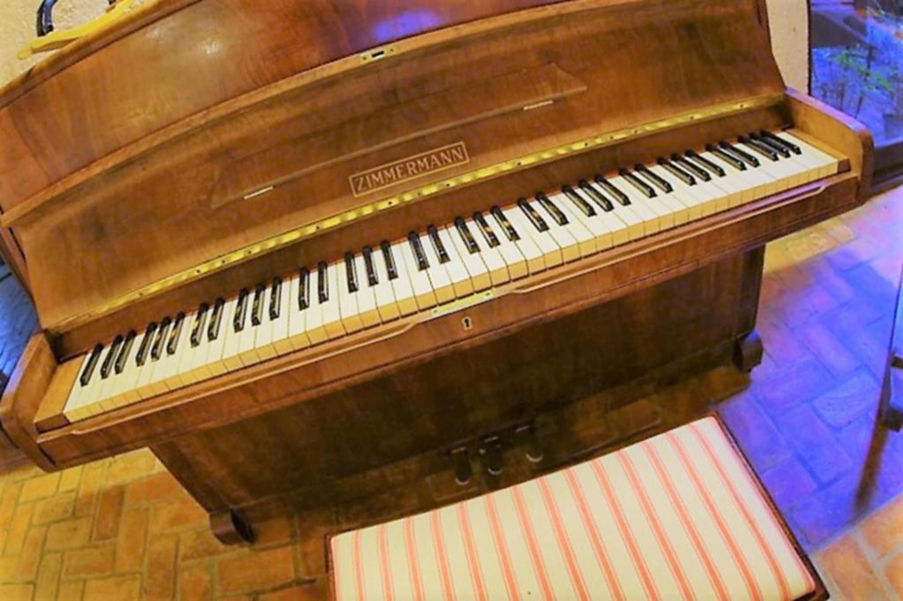 Um piano de cauda com acabamento em madeira e a marca "ZIMMERMANN" visível na lateral.