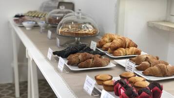 Buffet com diversos produtos de panificação, incluindo croissants, muffins e bolos.