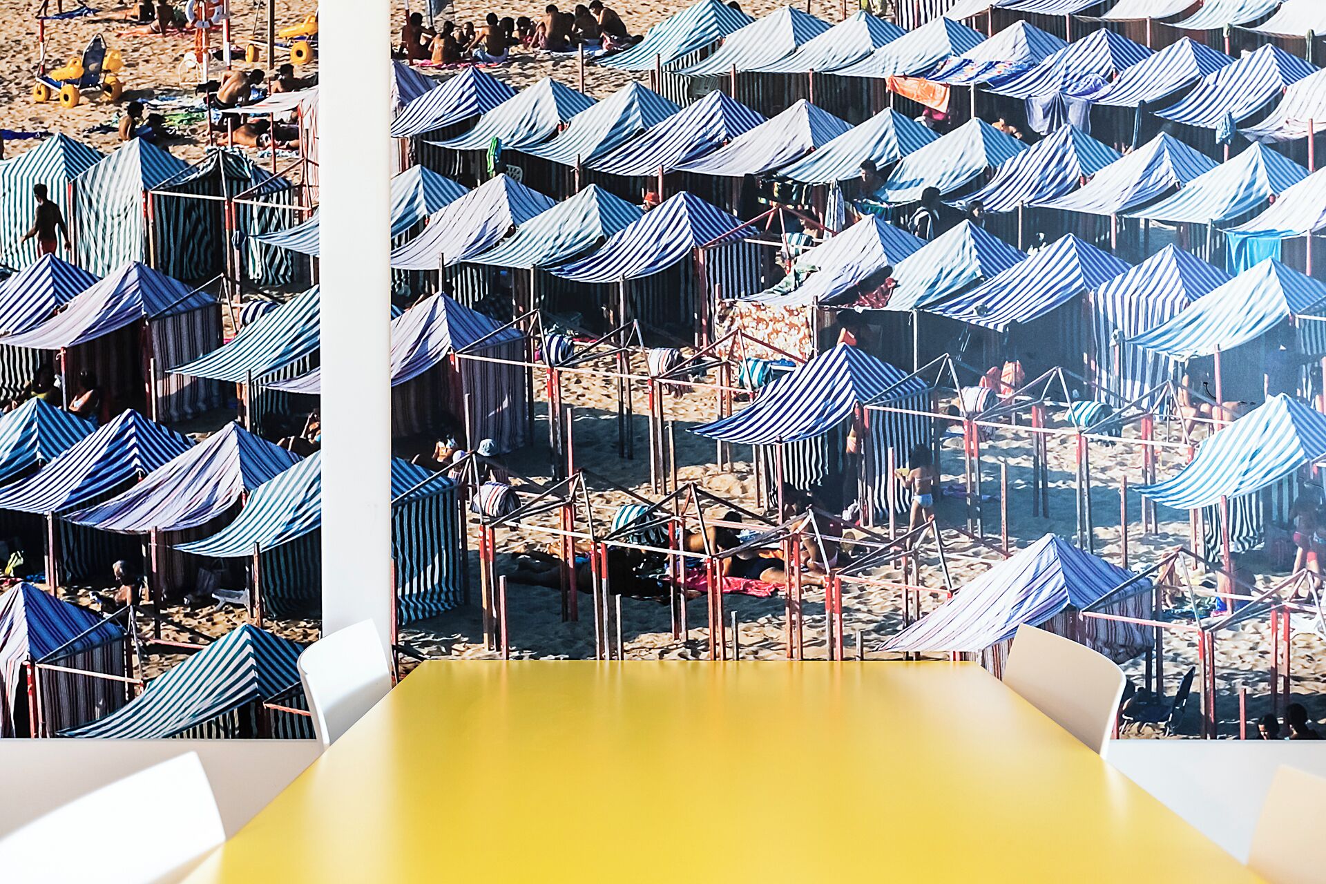 Uma praia com guarda-sóis listrados e uma mesa amarela em primeiro plano.