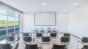 Uma sala de conferências com uma janela grande, uma tela de projetor e fileiras de cadeiras.