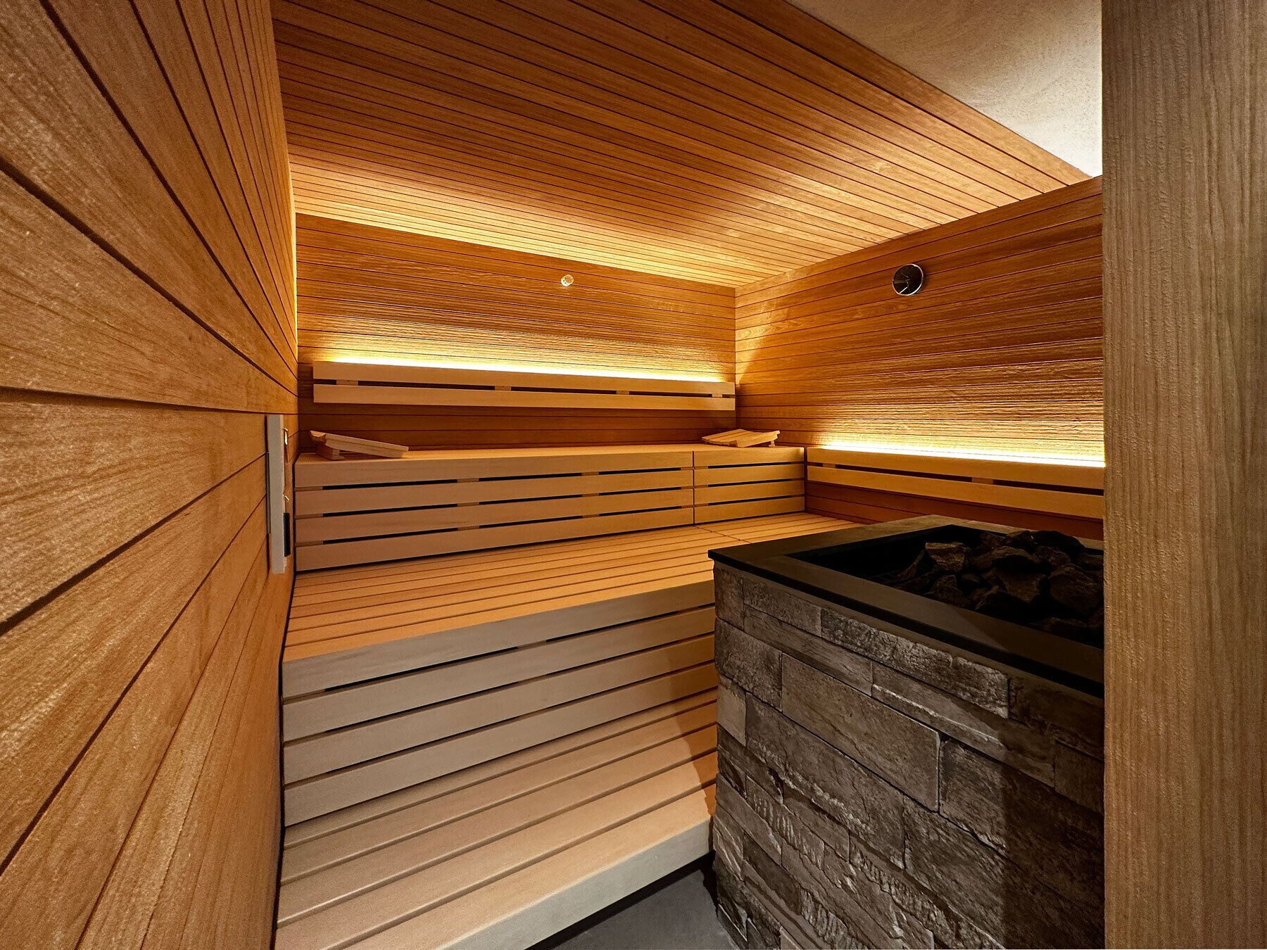 Uma sauna com ripas de madeira e um banco de pedra.