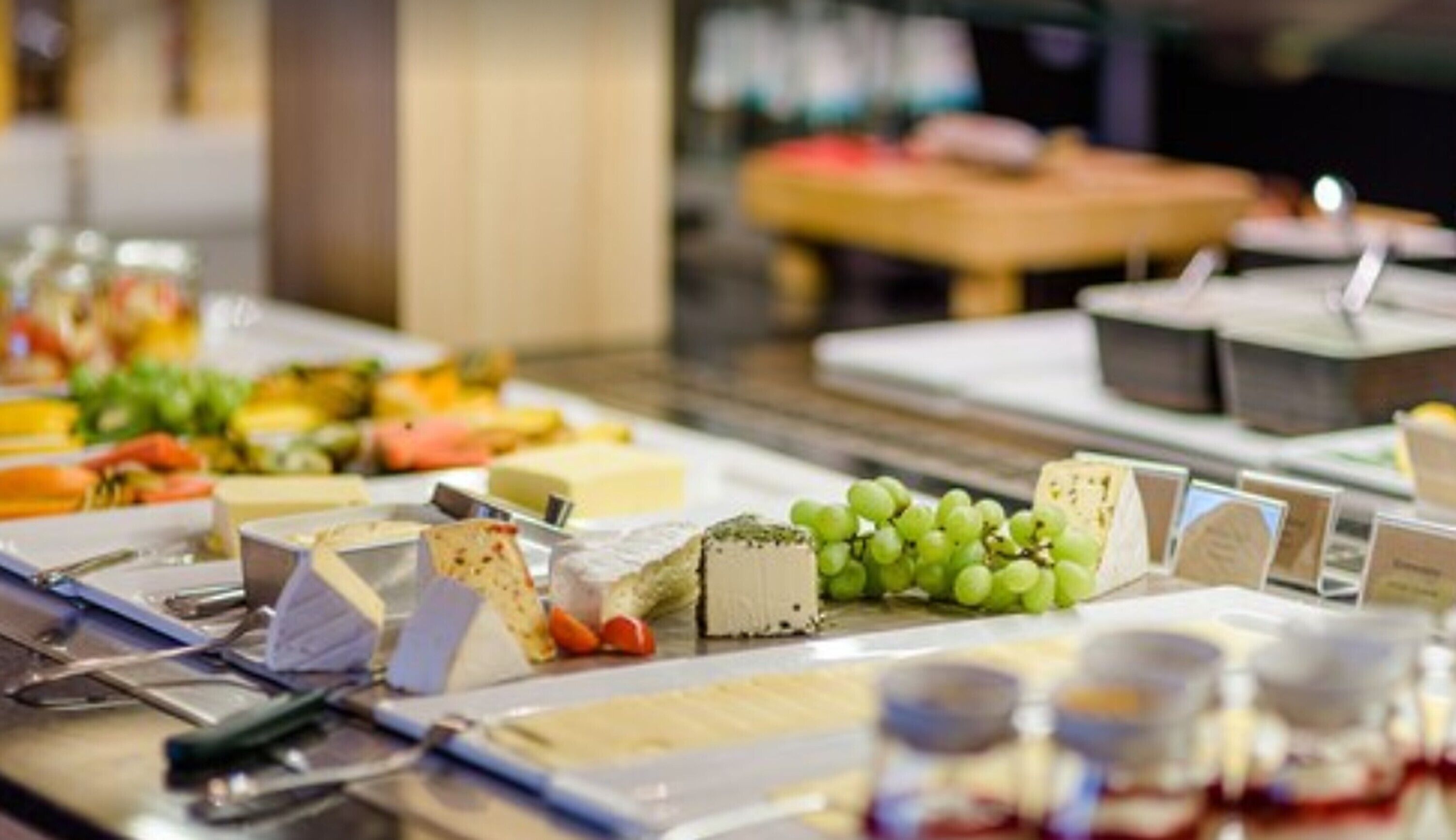 Um buffet com diversos queijos, frutas e uma variedade de bebidas.