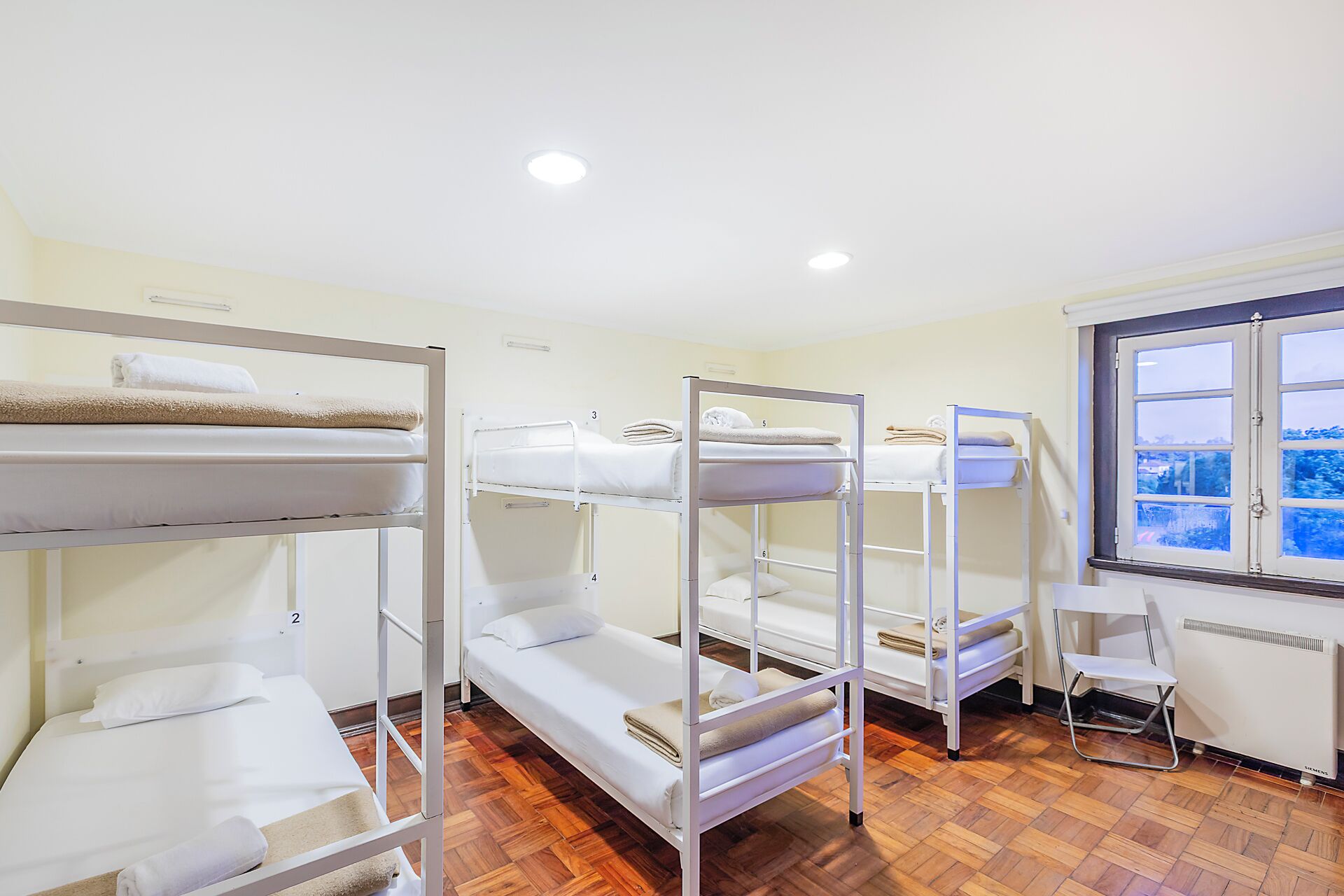 Um quarto tipo dormitório com beliches, uma janela com vista e um radiador.