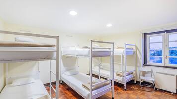 Um quarto tipo dormitório com beliches, uma janela com vista e um radiador.