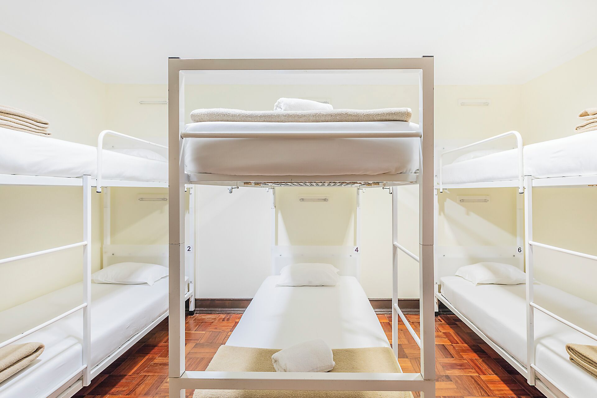 Quarto com beliche, roupa de cama branca e piso de madeira.