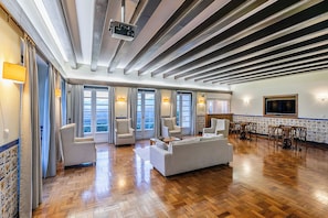 Uma sala de estar ampla com piso de madeira em padrão herringbone, um sofá, poltronas, uma televisão e um espaço bar com painel de azulejos.