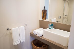 Uma casa de banho moderna com uma banheira branca, um espelho grande e um porta-toalhas com duas toalhas brancas.