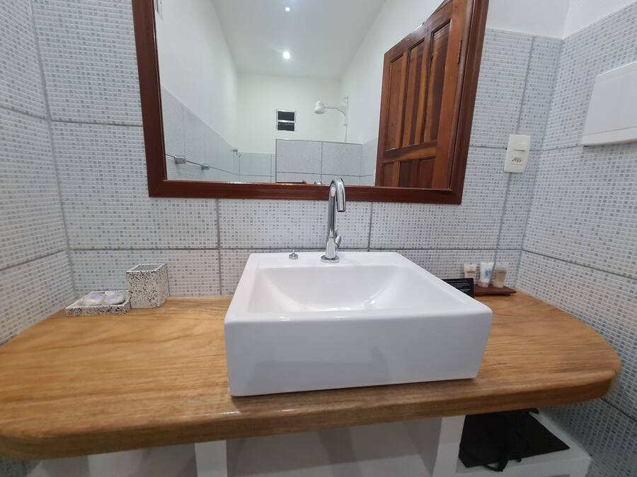 Casa de banho com lavatório branco, bancada de madeira e espelho em cima.