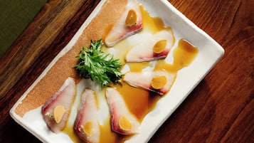 Prato retangular branco com uma porção de sashimi sobre uma mesa de madeira.