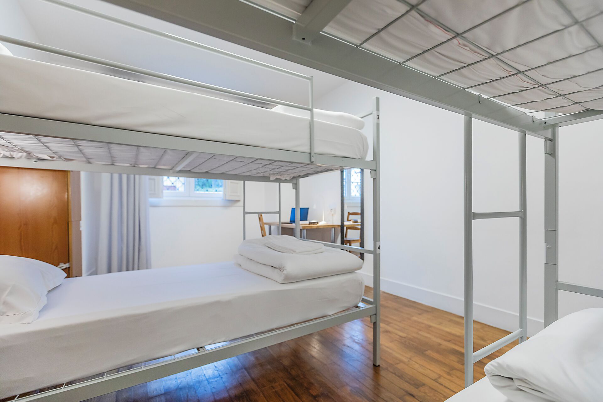 Quarto com beliche, escrivaninha e cadeira, janela e porta.