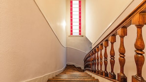 Uma escada de madeira com corrimão, uma janela com vidros vermelhos e uma parede com textura.
