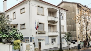 Um edifício branco com varandas, uma bandeira e um portão.