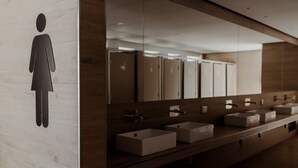 Uma casa de banho moderna com lavatório de madeira, várias pias e um símbolo de acesso unissexo na parede.