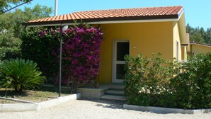 Um edifício amarelo com telhado de telhas vermelhas, porta de entrada e degraus que levam ao acesso.