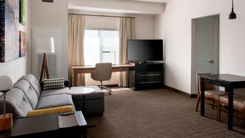 Quarto de hotel moderno com sofá, escrivaninha, televisão e mesa de jantar.