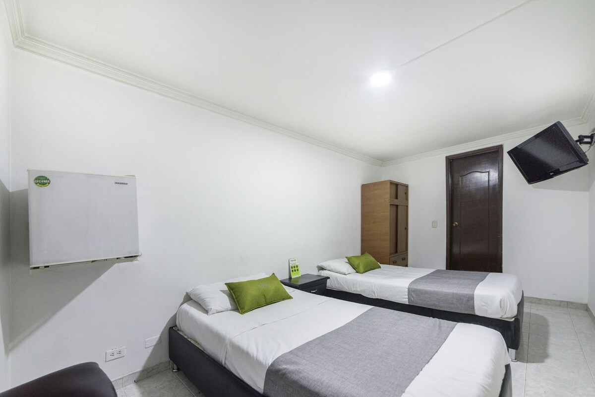 Quarto de hotel com duas camas, televisão, guarda-roupa e ar condicionado.