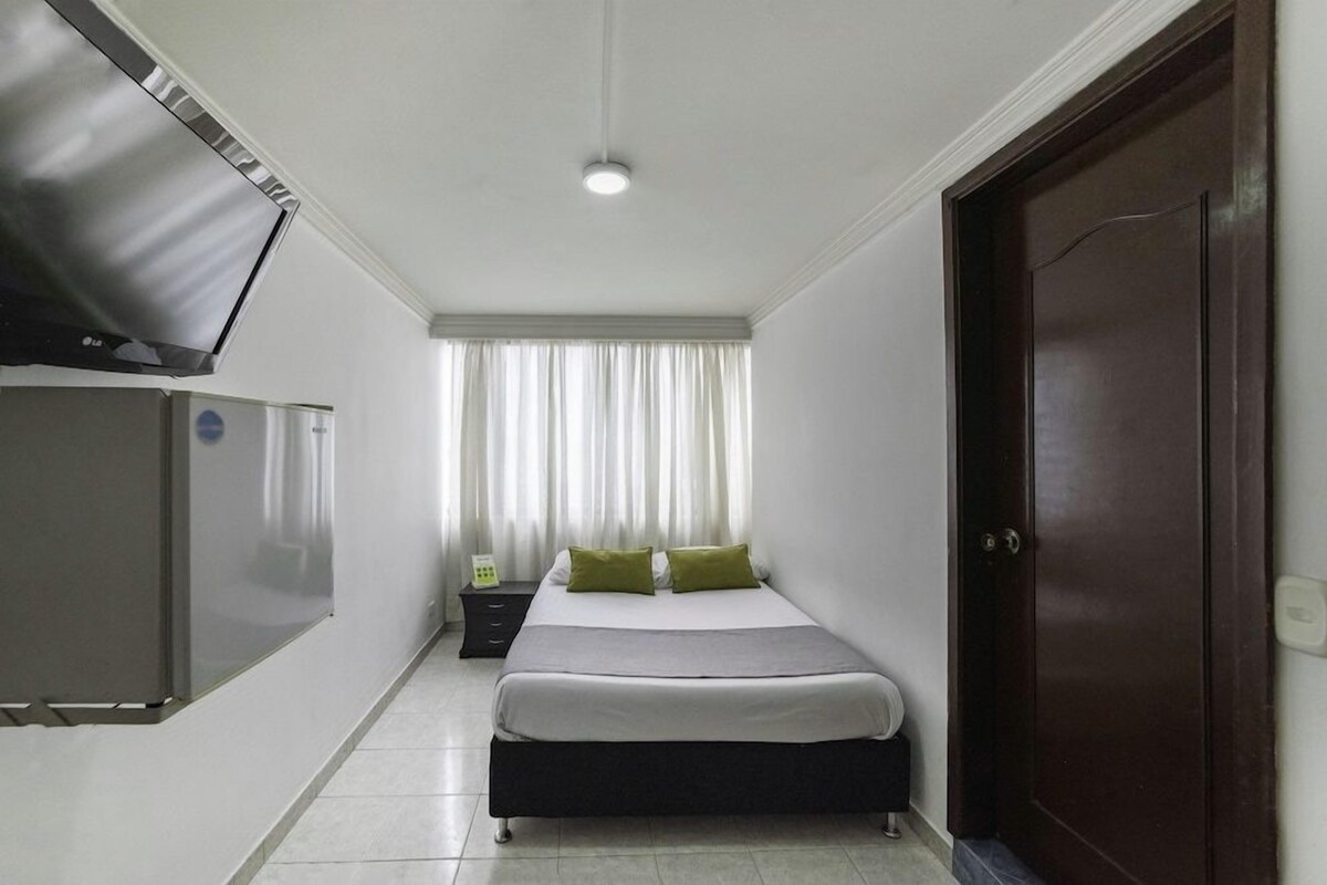 Quarto com cama, televisão, mesa de cabeceira e porta.